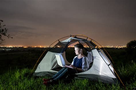 여자는 밤에 캠핑에 헤드셋과 함께 그녀의 노트북을 사용 하 여 여성 흐린 밤하늘 아래 텐트에 앉아 배경 발광 시에 경관에 대한 스톡 사진 및 기타 이미지 Istock