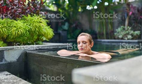 발리에서 열대 휴가 기간 동안 고급스러운 호텔의 햇볕이 잘 드는 무성한 돌 수영장에서 야외에서 휴식을 취하는 아름다운 평화로운 여성 앞마당 또는 뒷마당에 대한 스톡 사진 및