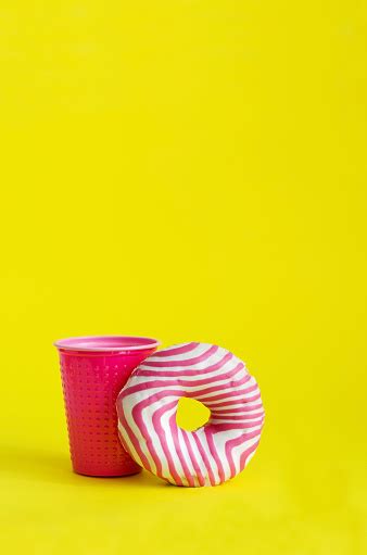 흰색 아이싱과 분홍색 선이 있는 도넛은 노란색 배경에 있는 작은 플라스틱 분홍색 유리 옆에 서 있습니다 수평 배경 부드러운 초점 0명에 대한 스톡 사진 및 기타 이미지