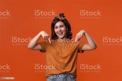 예쁜 갈색 머리 여자 에 티셔츠와 아름 다운 머리띠 가리키는 그녀의 손가락 아래로 오렌지 배경 위에 고립 된 광고를 위한