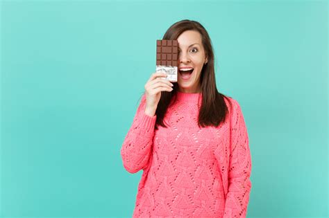 니트 핑크 스웨터 입 열어에 놀란된 젊은 여자 잡고 손 초콜릿 바 스튜디오에 파란색 벽 배경에 고립 된 덮 음 눈 사람들의 라이프 스타일 개념입니다 복사 공간을 비웃는 다