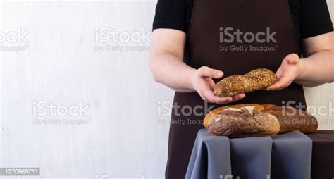 베이커는 신선한 호밀 빵을 보유하고 있습니다 복사 공간이있는 식탁보로 덮인 테이블에 갓 구운 빵의 다양한 건강한 음식과 전통적인 베이커리 컨셉 갈색에 대한 스톡 사진 및