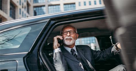 고급 자동차의 뒷좌석에 앉아있는 잘 생긴 고위 사업가 그는 차 문을 열고 나가거나 나간다 배경에 큰 버스가 부풀어 오른다 기업 비즈니스 개념의 교통 사진