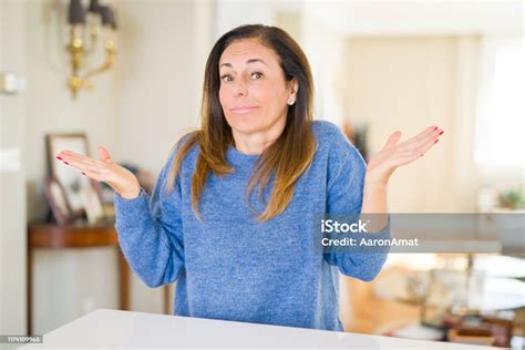 집에서 아름다운 중년 여성은 팔과 손을 들고 단서와 혼란스러운 표정을 합니다 의심 개념 어깨를 으쓱거림에 대한 스톡 사진 및 기타 이미지 어깨를 으쓱거림 한 명의