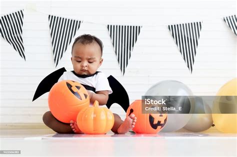 검은 박쥐 날개가있는 뱀파이어 멋진 할로윈 의상을 입은 사랑스러운 아프리카 아기 아이 쾌활한 작은 귀여운 아이는 오랑 호박 바구니를 들고 트릭이나 대접을하면서 파티에 간다