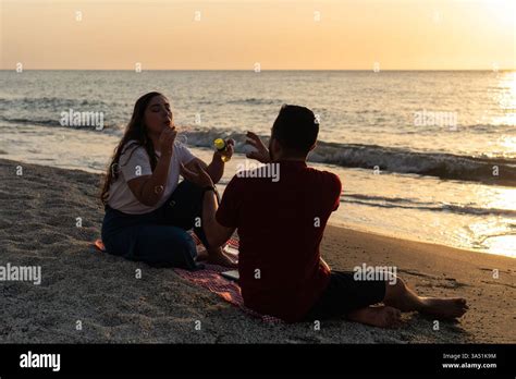 Couple Blowing Bubbles And Toasting On A Beach As The Sun Sets Stock