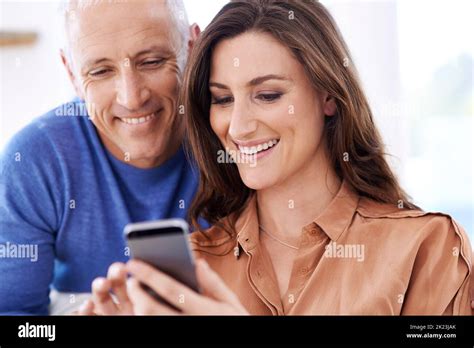 Checking Out Happy Holiday Snaps Together A Happy Mixed Age Couple Smiling At Messages On A