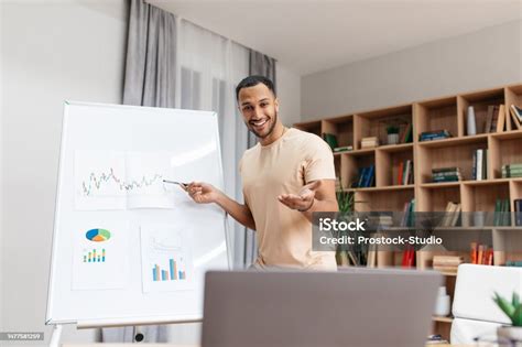 친절한 젊은 아랍 남자가 프로젝트 프레젠테이션을 만들고 온라인 회의 중에 화이트보드에 그래프를 시연합니다 25 29세에 대한