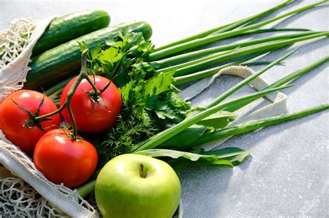 유기농 건강 식품 개념 신선한 생 채소와 과일이 있는 메쉬 식료품 백이 돌 콘크리트 테이블에 있습니다 토마토 사과 오이 파슬리에 대한 클로즈업 보기 0명에 대한 스톡 사진