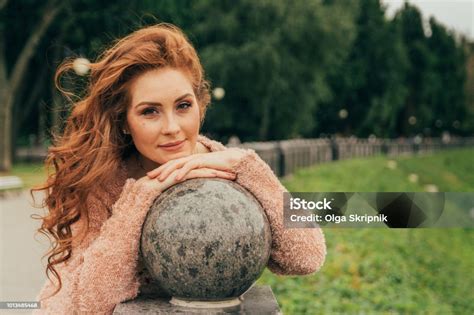 공원에서 화강암 공에 그녀의 팔꿈치를 기댄 아름 답 고 빨간 머리 여자의 초상화 바람 그녀의 곱슬 머리 아름 다운 머리카락을 개발 한다 여름 몽 상가에 꿈 여행 건강한 생활