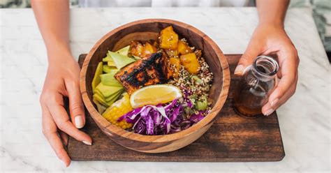 튀긴 연어 생선 스테이크 퀴노아 아보카도 옥수수 양배추 샐러드 구운 호박을 나무 그릇에 담아 식사를 하는 여자 건강한 유기농 식품 개념 흰색 대리석 테이블