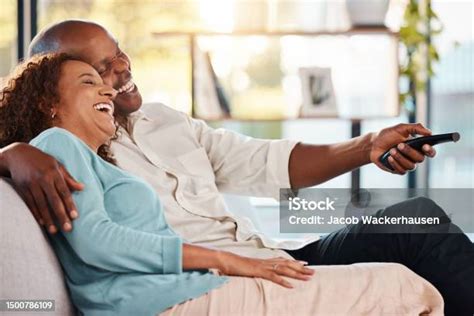부부는 Tv를 보고 소파에서 웃고 집 거실에서 포옹하고 유대감을 형성한다 인종 간 텔레비전 재미있는 흑인 남성과 여성은 소파에서 코미디 영화 만화 영화 또는 밈 비디오를