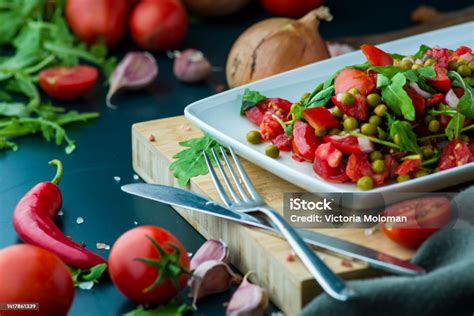 여름 샐러드 토마토 녹색 완두콩 Arugula 양파 올리브 오일 마늘 고추 포크 나이프 대나무 커팅 보드 파스텔 그린 냅킨 섬유 소금 채식주의 자 채식주의 자 음식 0명에