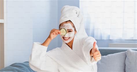 오이 조각을 들고 점토 얼굴 마스크를 쓴 젊은 여자 얼굴에 얼굴 마스크를 쓴 아름다운 젊은 여자가 신선한 오이 조각을 들고 있다 스킨 케어 및 트리트먼트 스파 자연의