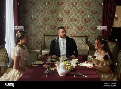 Group Scene At Dining Table Featuring Three Elegantly Dressed Figures