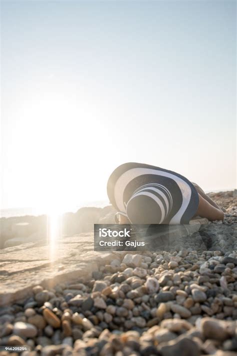 Woman Sunbathing On A Stony Beach Basking In The Hot Summer Sun In A