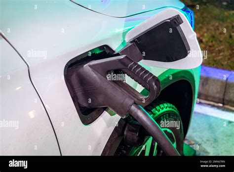 The White Car Is Connected To The Electric Charging Station At Night In Neon Lights Stock Photo