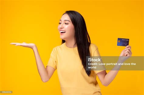 행복한 젊은 아시아 여자 플라스틱 신용 카드를 들고 손바닥과 복사 공간을 보고 만족 하 고 노란색 배경 위에 서 고객 소녀 도착 행복 의 신용 카드 서비스 의 얼굴 캐시백