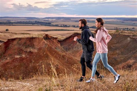 Athletic Male Female Jogging Along Field Outside The City At Sunset