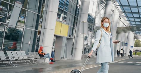 일회용 의료 마스크를 쓴 세련된 여성 관광객이 길 건너편에 있는 그녀의 트롤리 여행 가방을 몰고 있다 사진 Unsplash의 여행하다 이미지