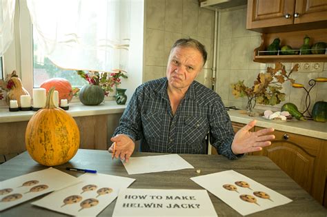 집에서 잭 오랜턴을 만드는 방법 한 중년 남성이 식탁에 앉아 호박을 자르는 방법을 고민합니다 10월에 대한 스톡 사진 및 기타 이미지 Istock