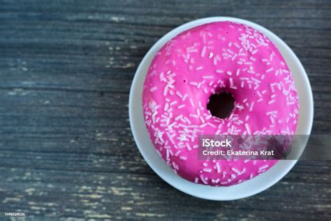 하얀 둥근 접시와 오래된 나무 회색 배경에 밝은 분홍색 도넛을 올려 놓으십시오 격리된 개체가 닫힙니다 아침 식사로 전통적인 미국 과자 복사 공간 위에 흰 설탕 장식입니다 0