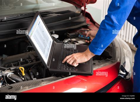 High Angle View Of Mechanic Examining Car Engine With Help Of Laptop ...