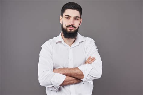 무기와 회색 벽에 기대어 잘생긴 젊은이 넘어 수염과 심각한 젊은 남자가 카메라에 보이는 가리키기에 대한 스톡 사진 및 기타