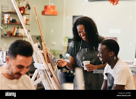 Cheerful Female Tutor With Young Student In Front Of Painting In Art