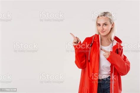 흰색 배경 위에 고립 된 왼쪽의 빈 공간에 손가락으로 가리키는 후드와 빨간 비옷에 금발 소녀 미소 광고 장소 가리키기에 대한 스톡 사진 및 기타 이미지 Istock