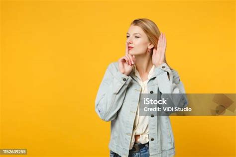 데님 캐주얼 옷에 호기심 젊은 여자는 입술 쉿 제스처에 손가락으로 조용 하 고 노란색 오렌지 벽 배경에 고립 듣기 위해 시도 말한다 사람들 라이프 스타일 개념입니다 복사