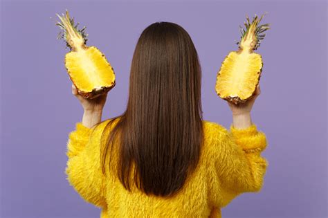 모피 스웨터에 젊은 갈색 머리 여자의 뒷 전망 보라색 파스텔 배경에 고립 된 신선한 잘 익은 파인애플 과일의 Halfs를 개최 합니다 사람들은 생생한 라이프 스타일 휴식
