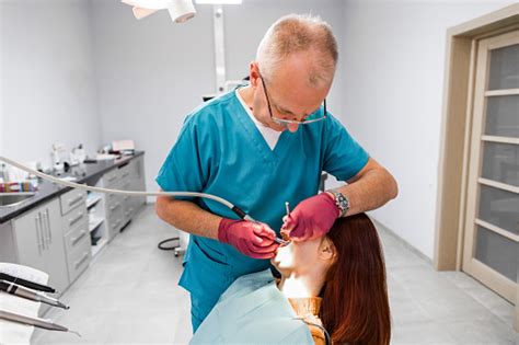 현대 빛 치과 진료소에서 젊은 여성 환자의 치아를 치료하는 파란색 유니폼과 장갑을 착용한 수석 전문 남성 의사 치과 의사의 초상화 2명에 대한 스톡 사진 및 기타 이미지