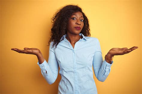 고립 된 노란색 배경에 우아한 셔츠를 입고 아프리카 계 미국인 사업가는 팔과 손을 들고 단서와 혼란스러운 표정을 지었습니다 의심