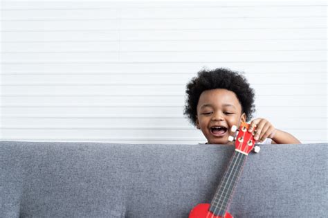 집에서 소파에 우쿨렐레 또는 작은 기타와 함께 연주 아프리카 계 미국인 어린 소년 쾌활한 귀여운 아프리카 계 미국인 어린 소년 즐거운 재미 즐기고 개념을 재생 2 3 살에