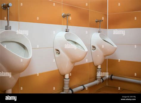 Restroom Interior With White And Orange Ceramic Tiles On The Walls And A Row Of Sanitary Ware