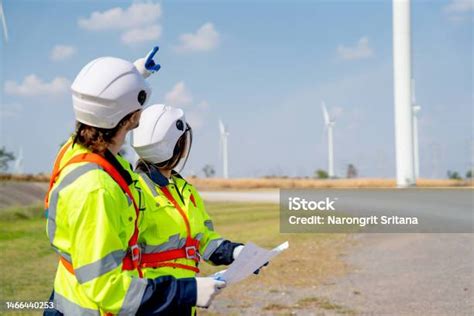 백인 엔지니어 남자와 여자의 뒤는 여자와 함께 그림 종이를 들고 푸른 하늘이 있는 풍차 또는 풍력 터빈의 줄 앞에 머물러 있습니다 20 24세에 대한 스톡 사진 및 기타