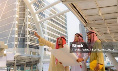 아랍 스타일을 입고 건축과 건물을 점검하는 청사진을 들고 서있는 두 명의 젊은 무슬림 엔지니어와 아랍 사업가 남자 사업가에 대한