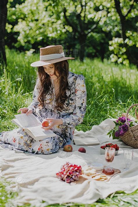 一名年轻女子戴着草帽，穿着夏装，在公园里悠闲地看书素材 花瓣网