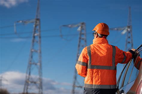 Construction Worker Surveys Electrical Infrastructure With Electrical Pylons Blue Sky