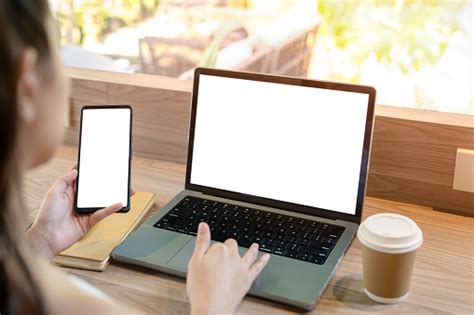 스마트폰과 노트북을 사용하는 여성의 어깨 너머로 보이는 모습 빈 흰색 화면 시뮬레이션 Brand Name Smart Phone에 대한 스톡 사진 및 기타 이미지