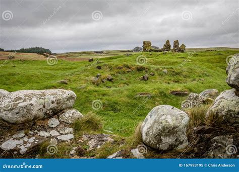 A Few Rounded Stones With Scrubby Grass In The Foreground And The Ruins