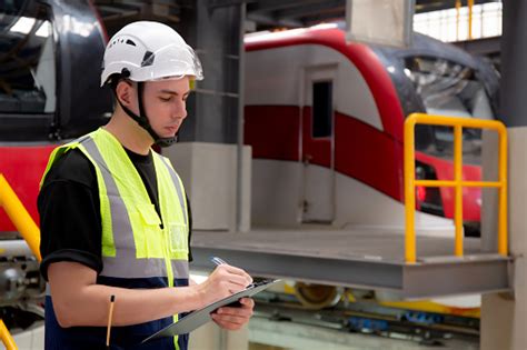 젊은 엔지니어 또는 노동자는 역 운송 및 인프라에서 유지 보수 및 클립보드에 문서 작성을 위해 전기 열차를 점검하고 검사관이 서비스 운송을 확인합니다 건설 산업에 대한 스톡