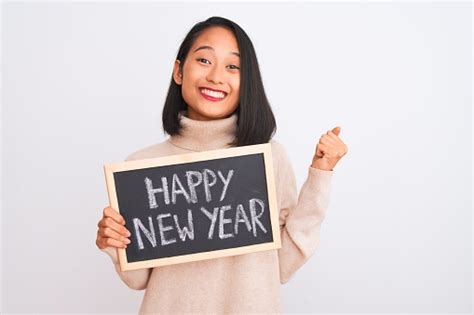 고립된 흰색 배경 위에 칠판을 들고 있는 젊은 아름다운 중국 여성은 자랑스럽고 승리와 성공을 축하하며 매우 흥분하고 환호하는 감정을 자랑합니다 감정에 대한 스톡 사진 및