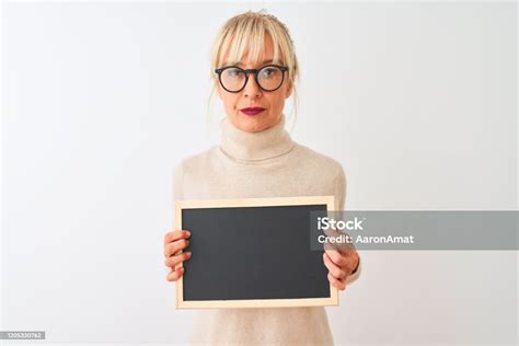 고립된 흰색 배경 위에 칠판을 들고 안경을 쓰고 있는 중년 여성이 스마트한 얼굴에 자신감 있는 표정을 지니고 있습니다 감정에