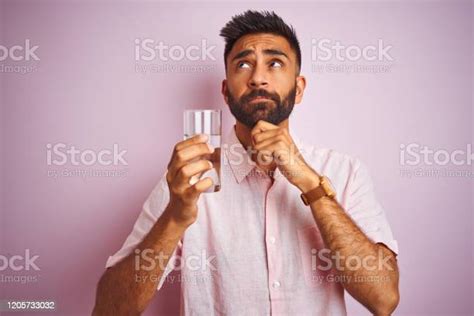 젊은 잘 생긴 인도 남자 Dinking 유리 위에 고립 된 분홍색 배경 심각한 얼굴 생각 에 대 한 질문 매우 혼란 스러운 아이디어 유리잔에 대한 스톡 사진 및 기타 이미지