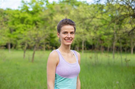 공원에서 조깅 하는 스포티 한 갈색 머리 소녀의 초상화입니다 배경에 녹색 숲입니다 프레임과 미소를 짓고 있는 스포츠 탑을 입은