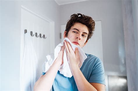 여드름 문제가있는 집중된 백인 십대 소년은 집에서 얼굴 피부를 돌 봅니다 그는 거울을보고 욕실에서 수건으로 얼굴을 닦습니다 십대 피부 관리 매일 치료 과정 16 17 살에