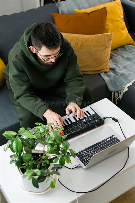 Man Recording Electronic Music Track With Portable Midi Keyboard On Laptop Computer In Home
