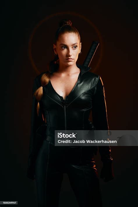 어두운 스튜디오에서 액션 싸움 위험으로부터의 안전을 위해 스튜디오에서 여성 전사 및 패션 의상을 입습니다 공상 과학 가죽 코스프레 의상을 입은 강력한 여성 모델 암살자 또는